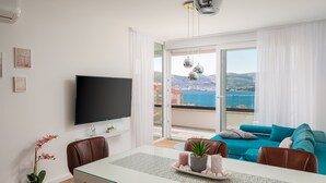 Uma sala de estar moderna com televisão de tela plana, uma mesa de jantar e um sofá com vista para o mar.