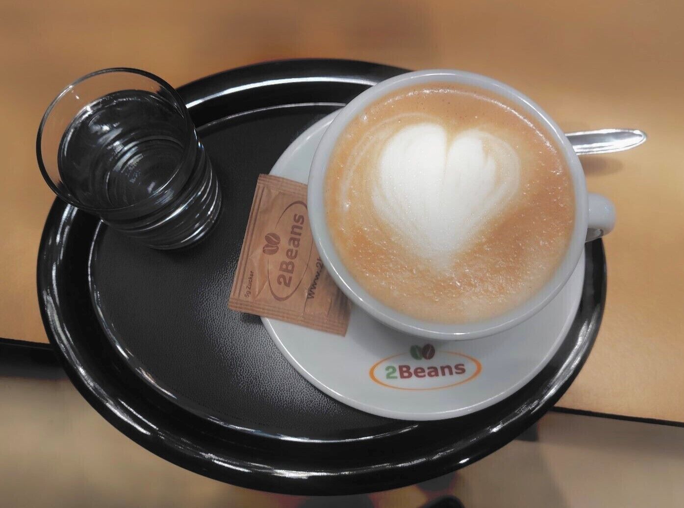 Uma chávena de café com arte de latte em formato de coração sobre um tabuleiro preto com um logótipo.