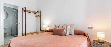 Quarto com cama grande, mesa de cabeceira com luminária, guarda-roupa e chuveiro em vidro.