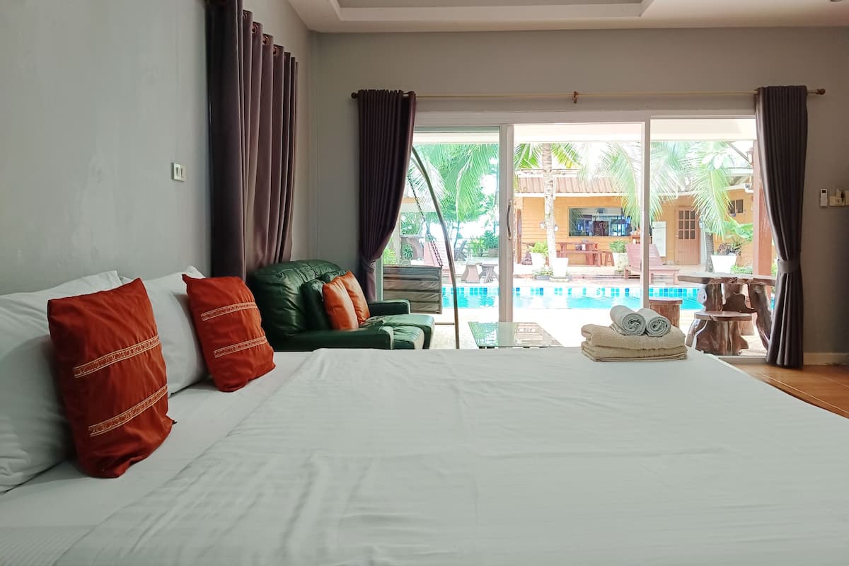 Quarto de hotel com uma cama grande, uma poltrona verde e vista para a área da piscina.