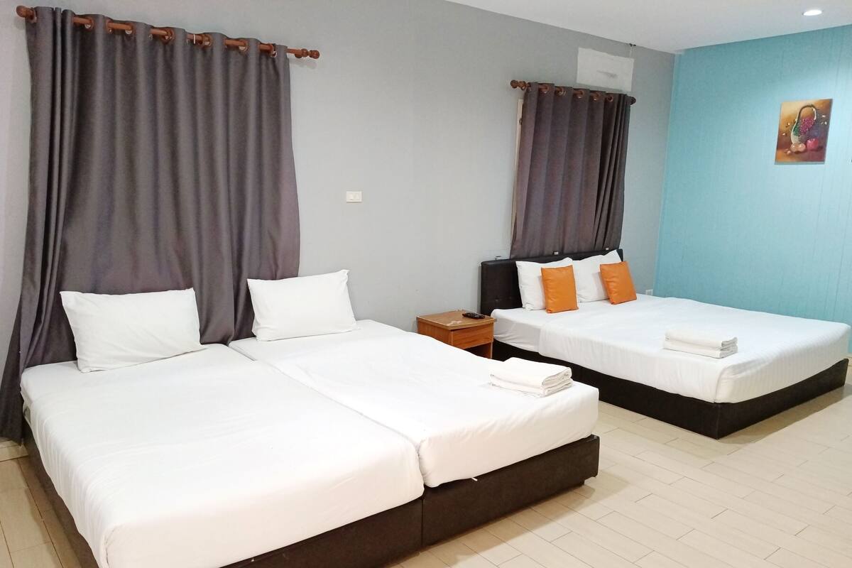 Quarto de hotel com duas camas, cortinas cinzentas, roupa de cama branca e uma pequena mesa de cabeceira de madeira.