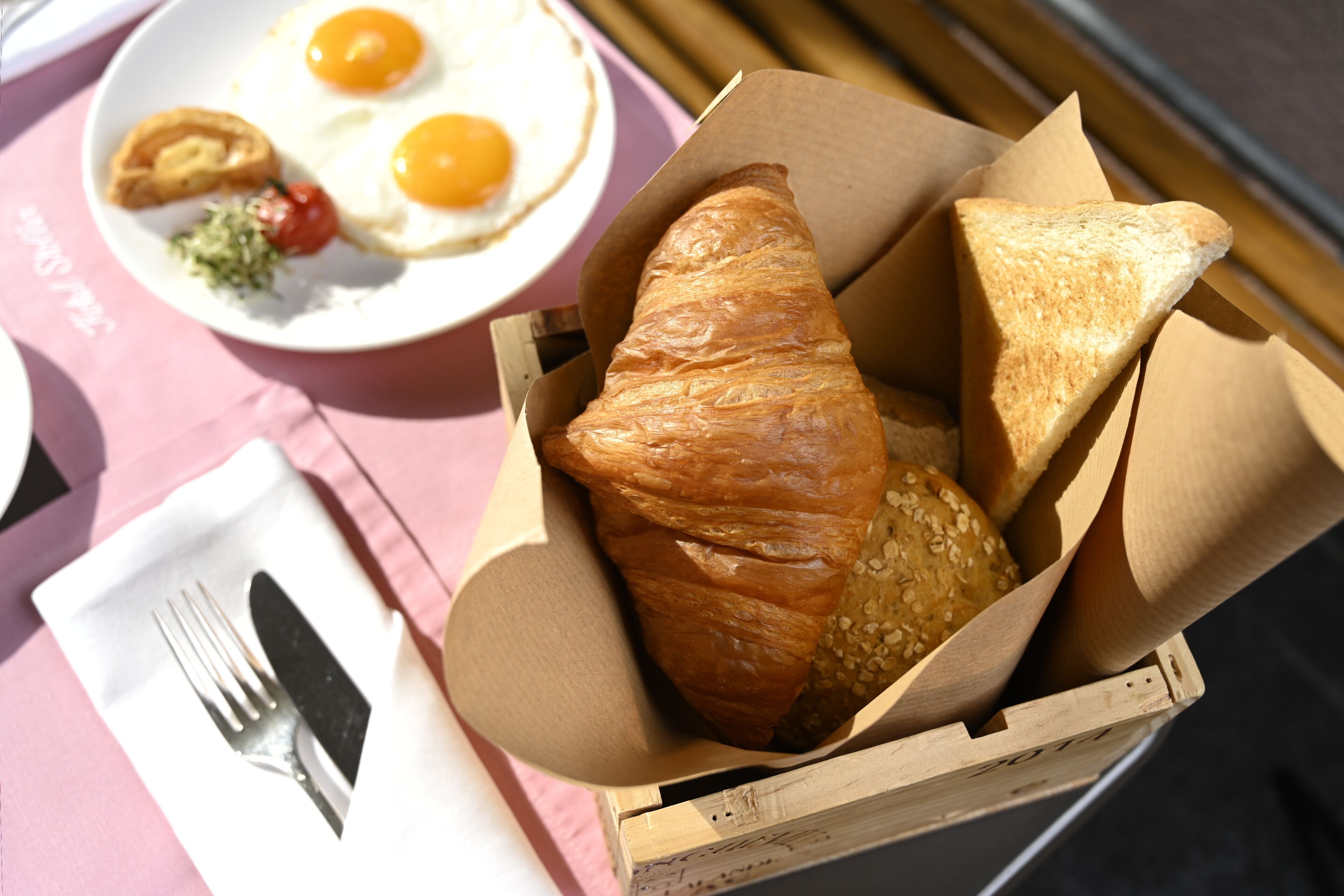 Caixa de madeira com um croissant, uma fatia de pão e um pequeno prato com ovos e tomate.