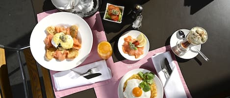 Uma mesa com itens de café da manhã, incluindo ovos, salmão defumado e torradas, junto com café e um copo de suco de laranja.
