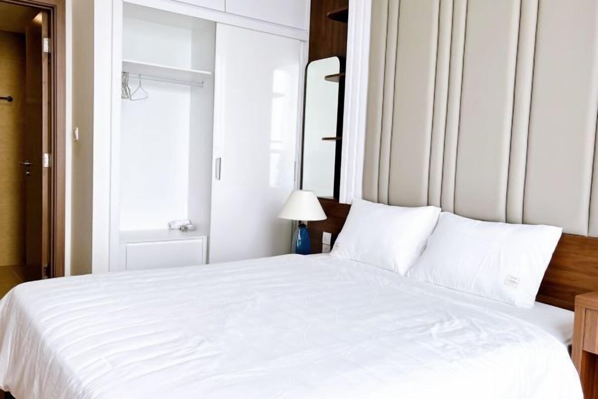 Quarto de hotel com uma cama grande, um guarda-roupa, um espelho e uma mesa de cabeceira.
