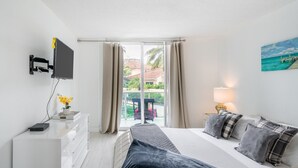 Quarto de hotel com cama, televisão fixada na parede, escrivaninha com luminária e vista para o exterior.