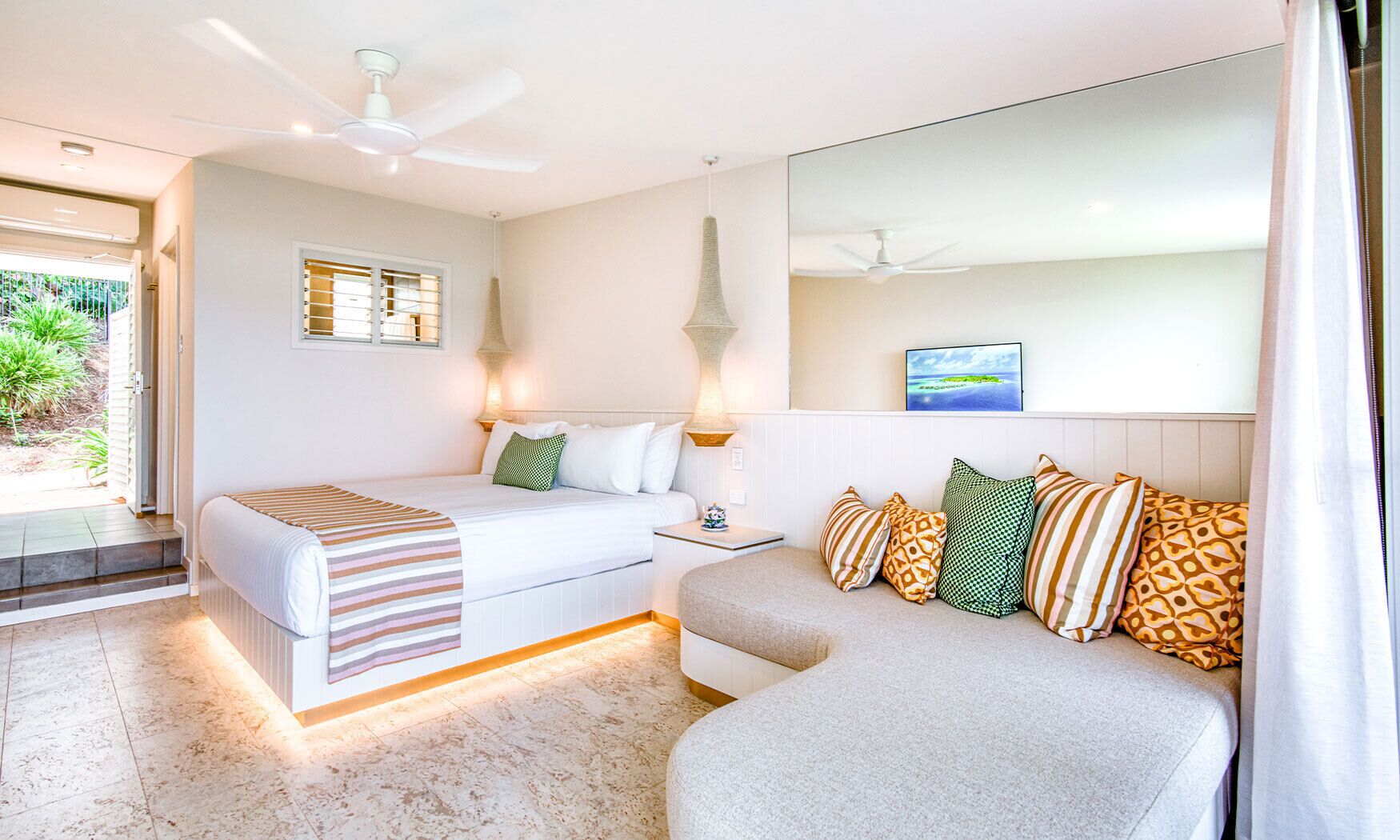Quarto moderno com cama, sofá, ventoinha no teto e uma janela grande.