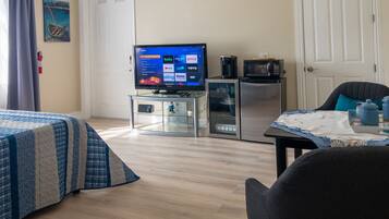 Quarto de hotel com cama, escrivaninha, computador, televisão, micro-ondas e frigorífico.