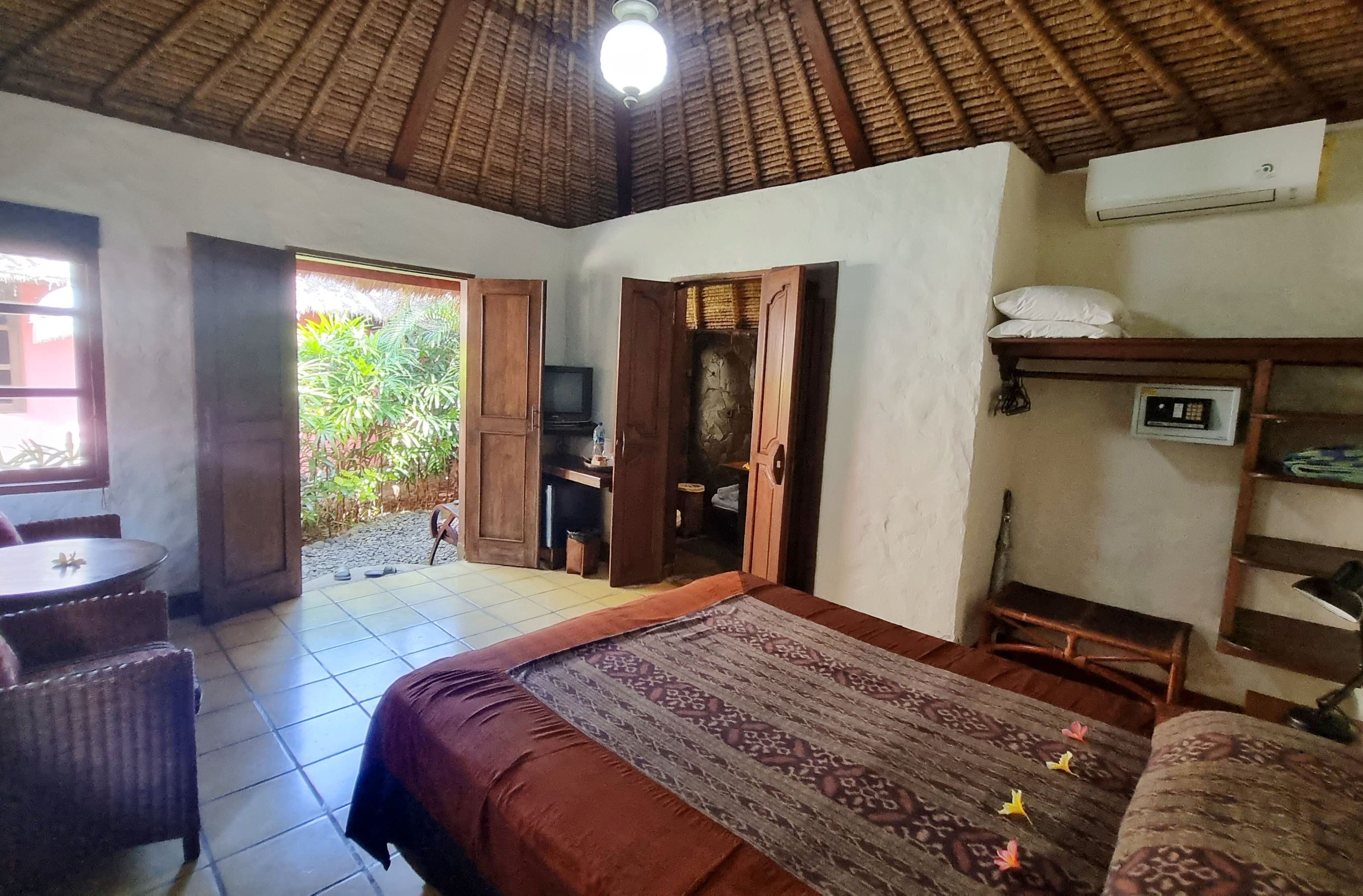 Quarto com uma cama, uma mesinha, uma cadeira, ar condicionado e uma televisão.