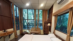 Quarto de hotel com cama grande, mobiliário de madeira e janelas amplas com vista para árvores.