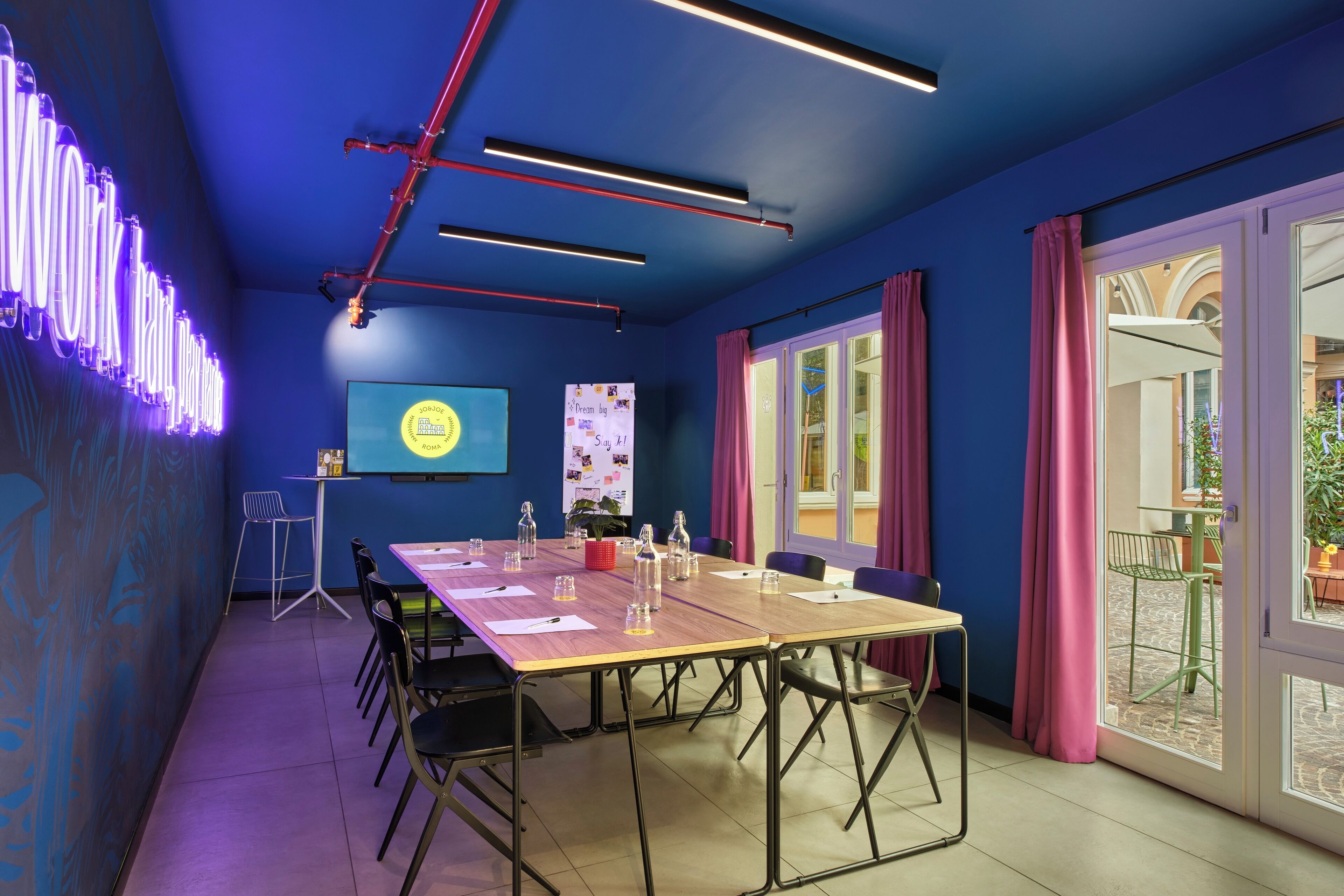 Sala de conferências com uma mesa grande, cadeiras, tela de projetor e uma janela com cortinas.
