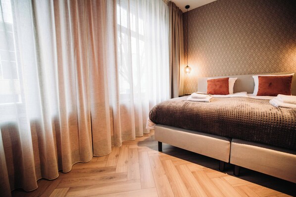 Quarto de hotel com cama grande, piso de madeira e parede estampada.