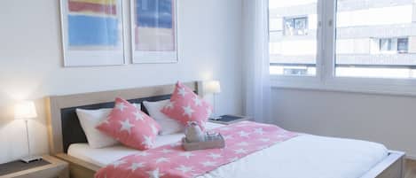 Um quarto com cama, mesas de cabeceira, abajur, janela e obras de arte na parede.