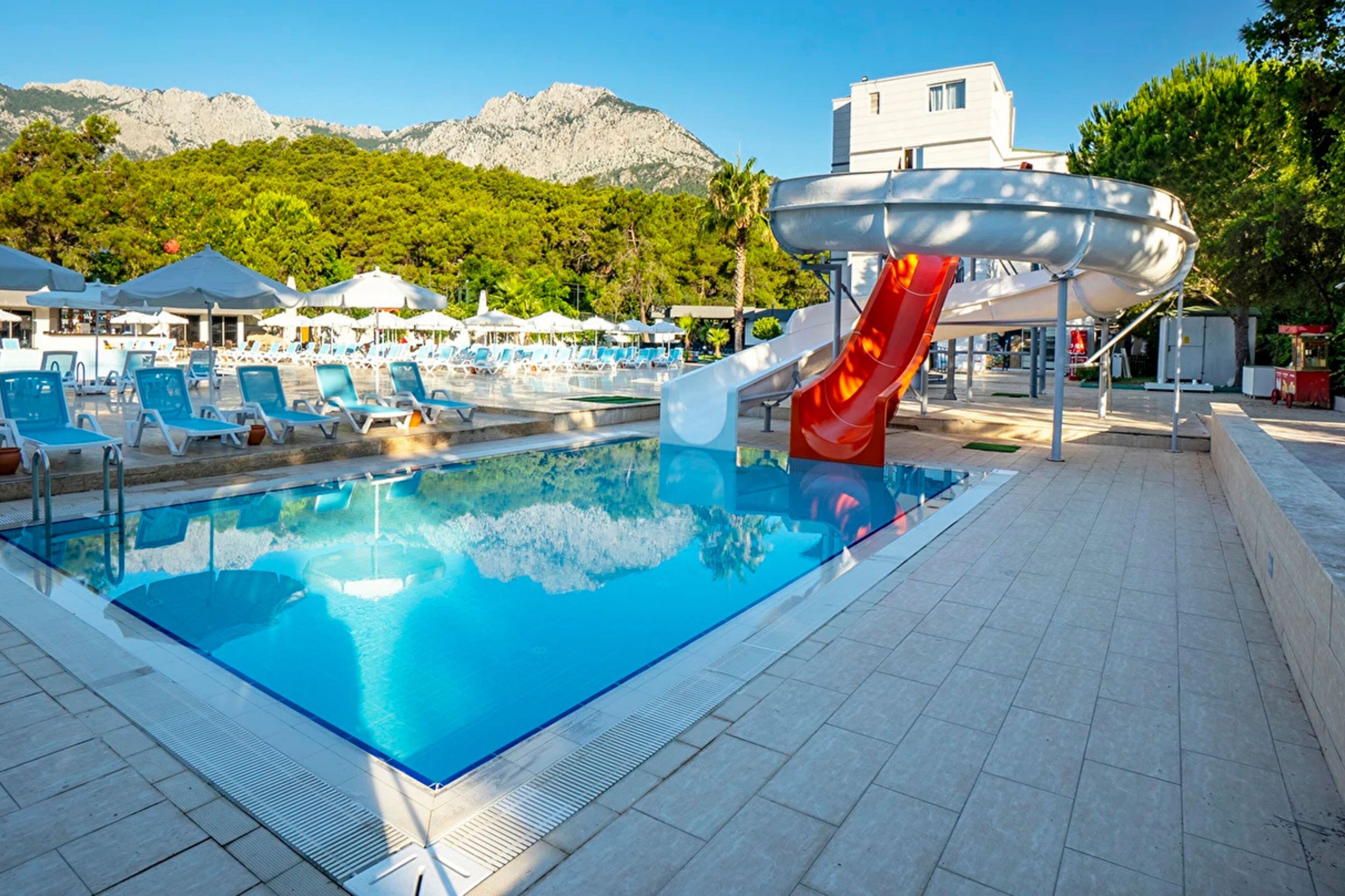 Uma piscina com escorregador, espreguiçadeiras e guarda-sóis.