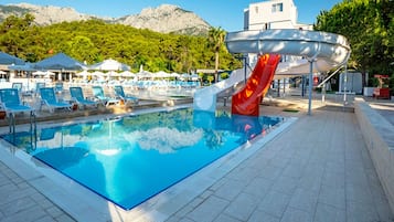 Uma piscina com escorregador, espreguiçadeiras e guarda-sóis.