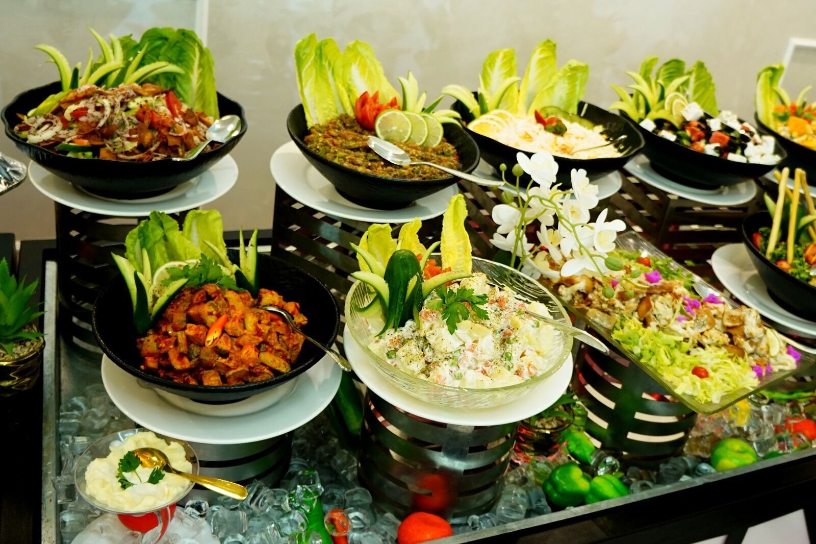 Buffet com diversos pratos, incluindo saladas, arroz e carnes, disposto sobre uma mesa com gelo e decorado com legumes frescos.