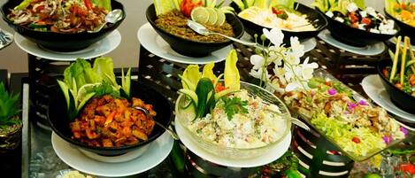 Buffet com diversos pratos, incluindo saladas, arroz e carnes, disposto sobre uma mesa com gelo e decorado com legumes frescos.