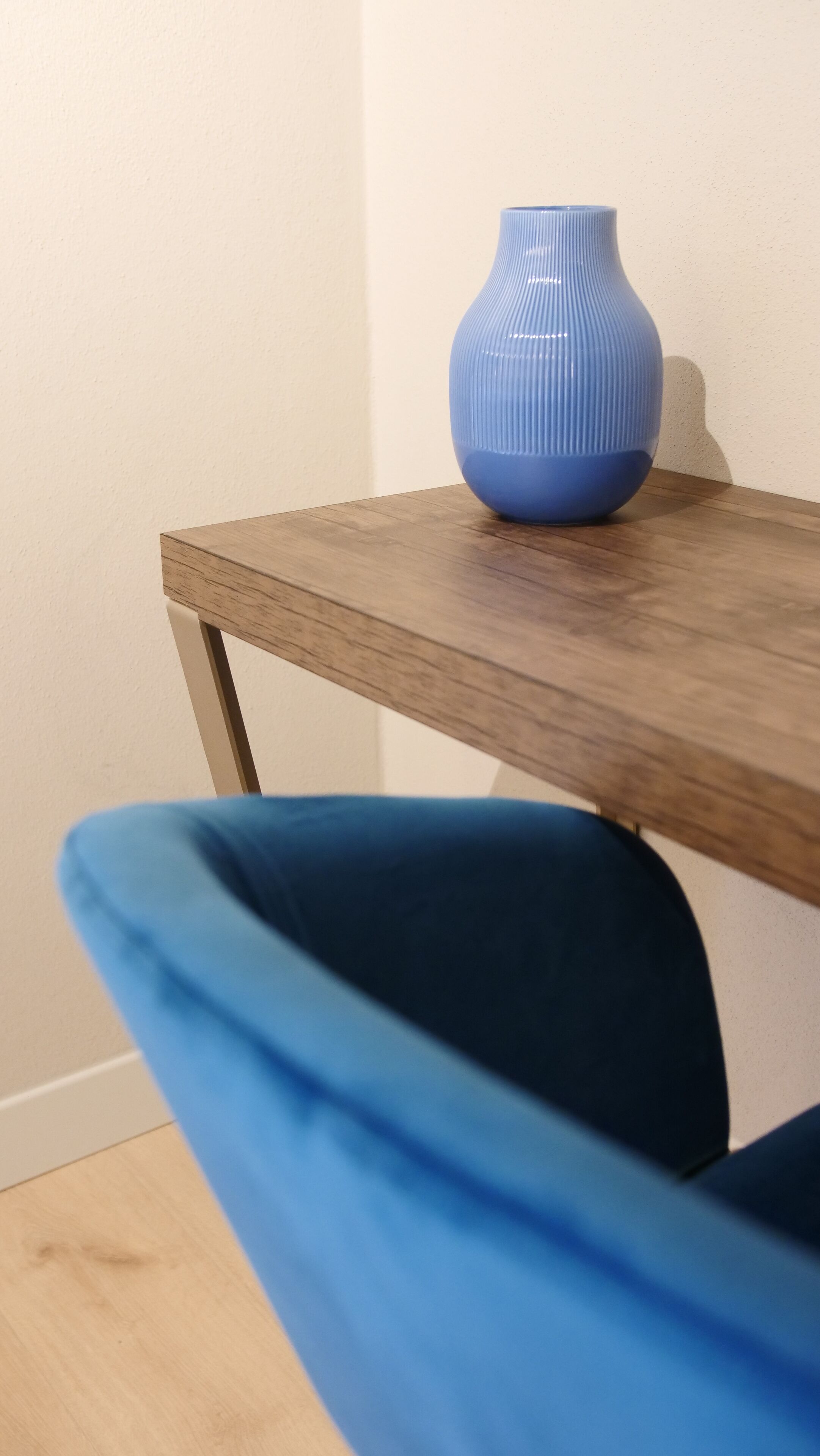 Uma cadeira azul e um vaso azul sobre uma mesa de madeira em frente a uma parede.