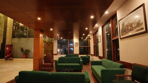 Um hall de hotel com sofás verdes, piso de madeira e grandes janelas.