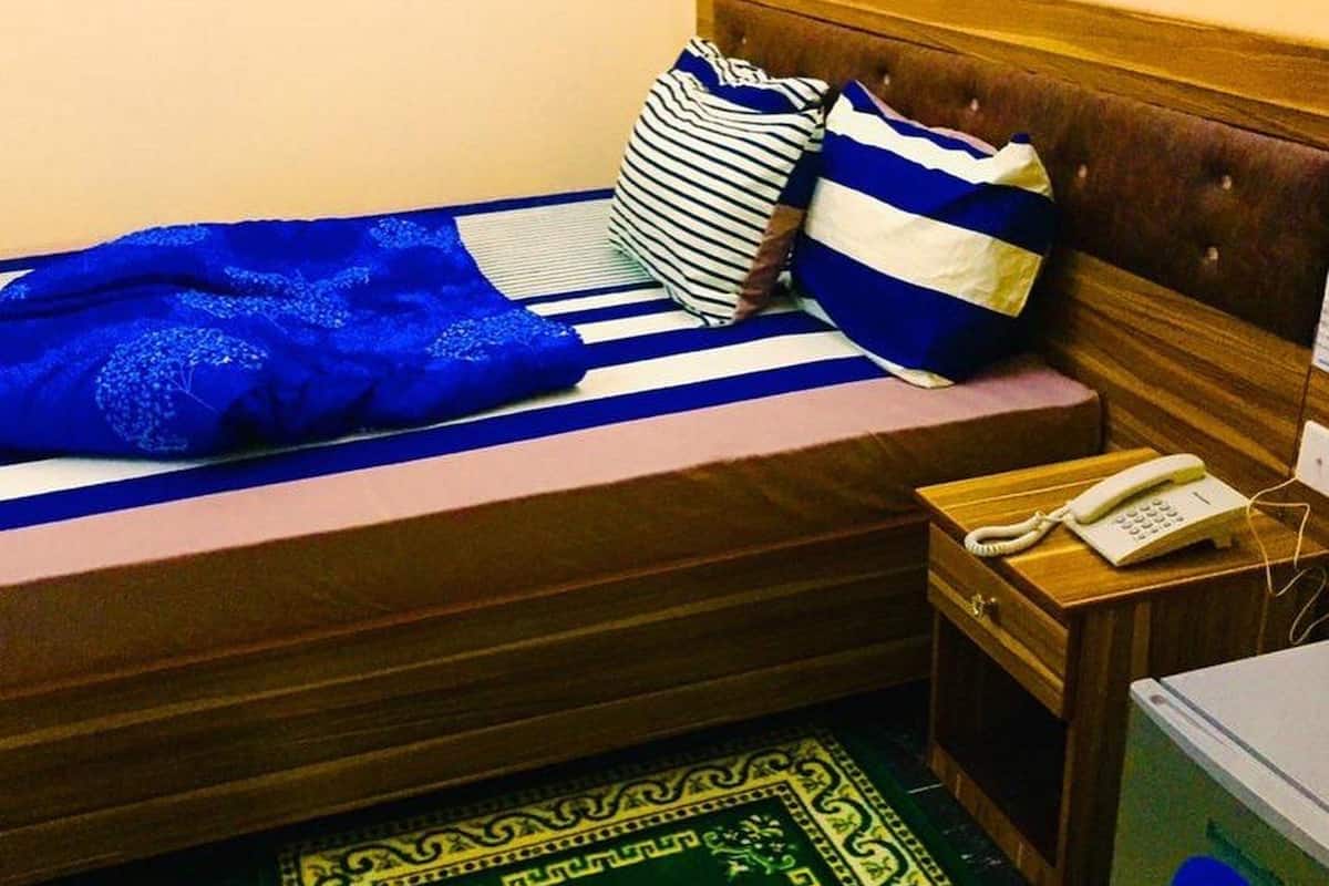 Quarto com cama, mesa de cabeceira com telefone e tapete verde estampado.
