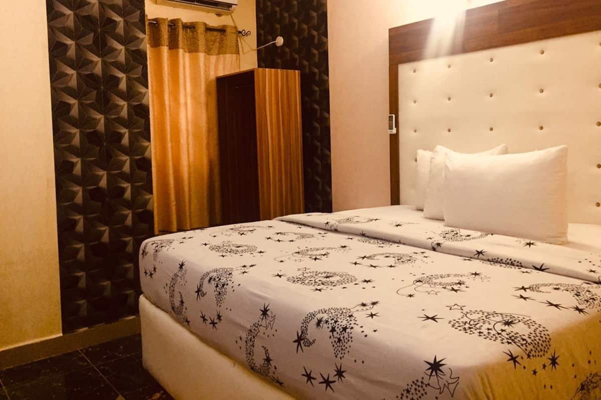 Quarto de hotel com cama, cabeceira, janela com cortinas e ar condicionado.