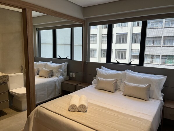 Quarto de hotel com cama, banheiro e uma grande janela.