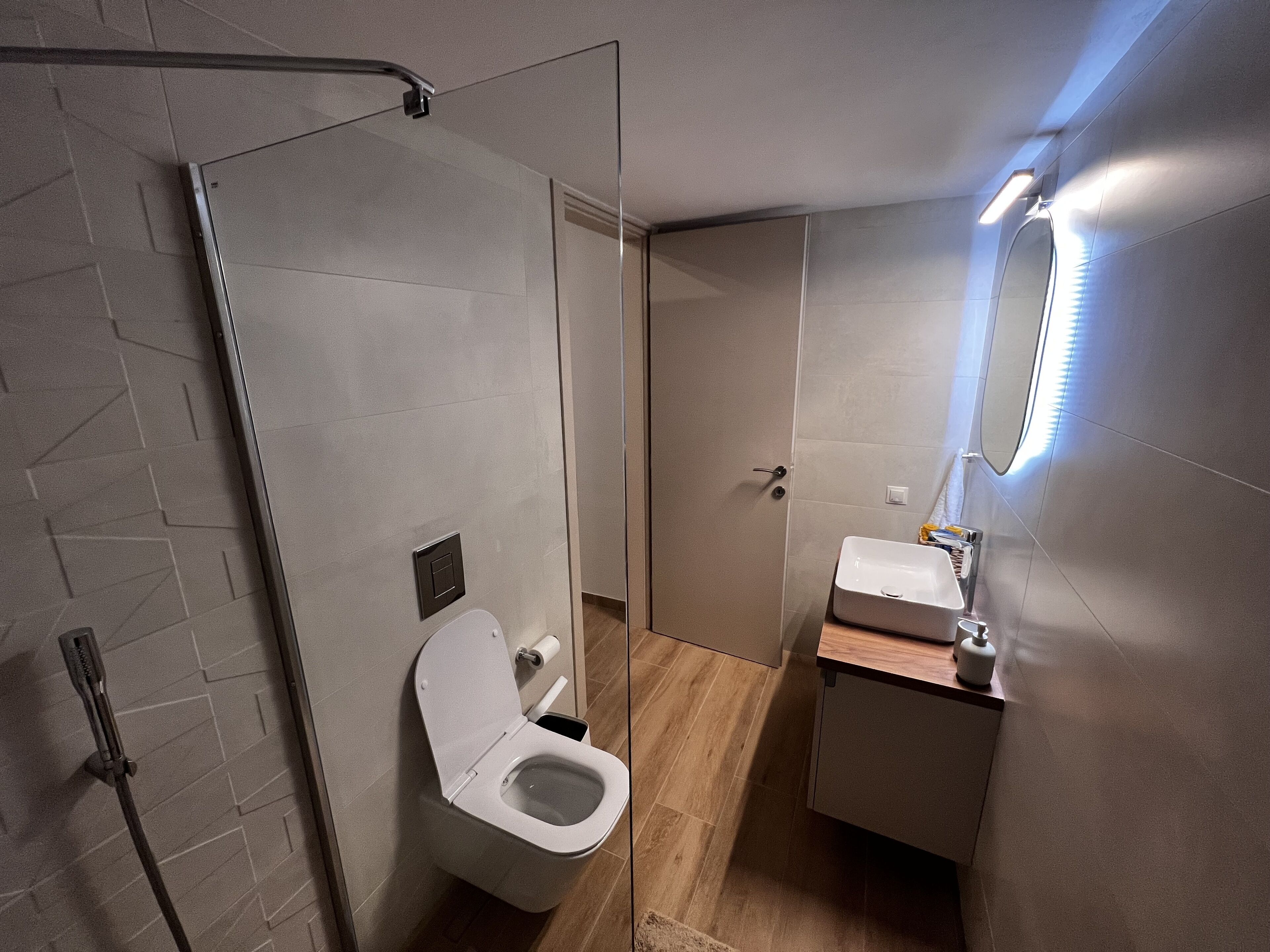 Uma casa de banho moderna com cabine de duche em vidro, sanita e lavatório com espelho.