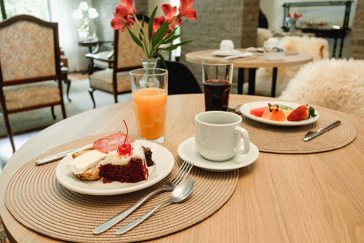 Uma mesa de jantar com um prato de comida, um copo de suco de laranja e uma xícara de café.