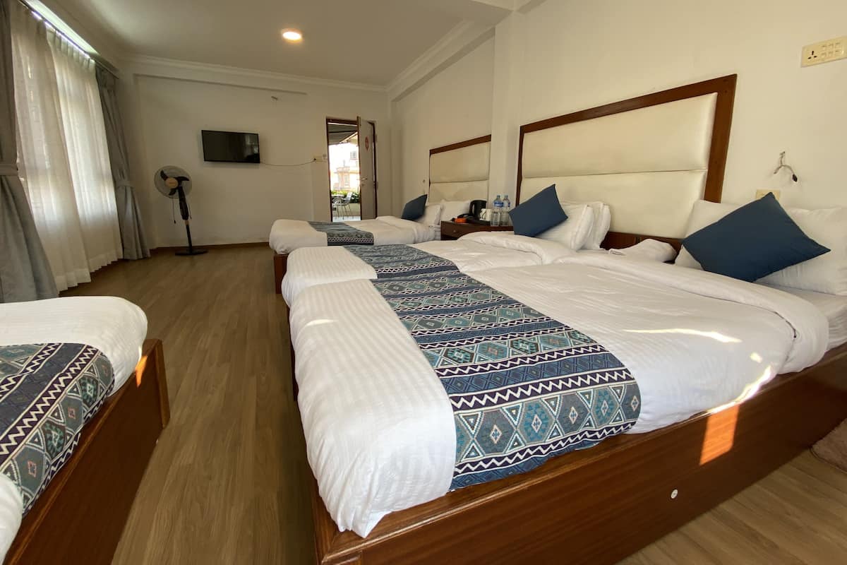 Quarto de hotel com uma cama grande, uma mesa de cabeceira, uma cadeira, um ventilador e vista para o exterior.