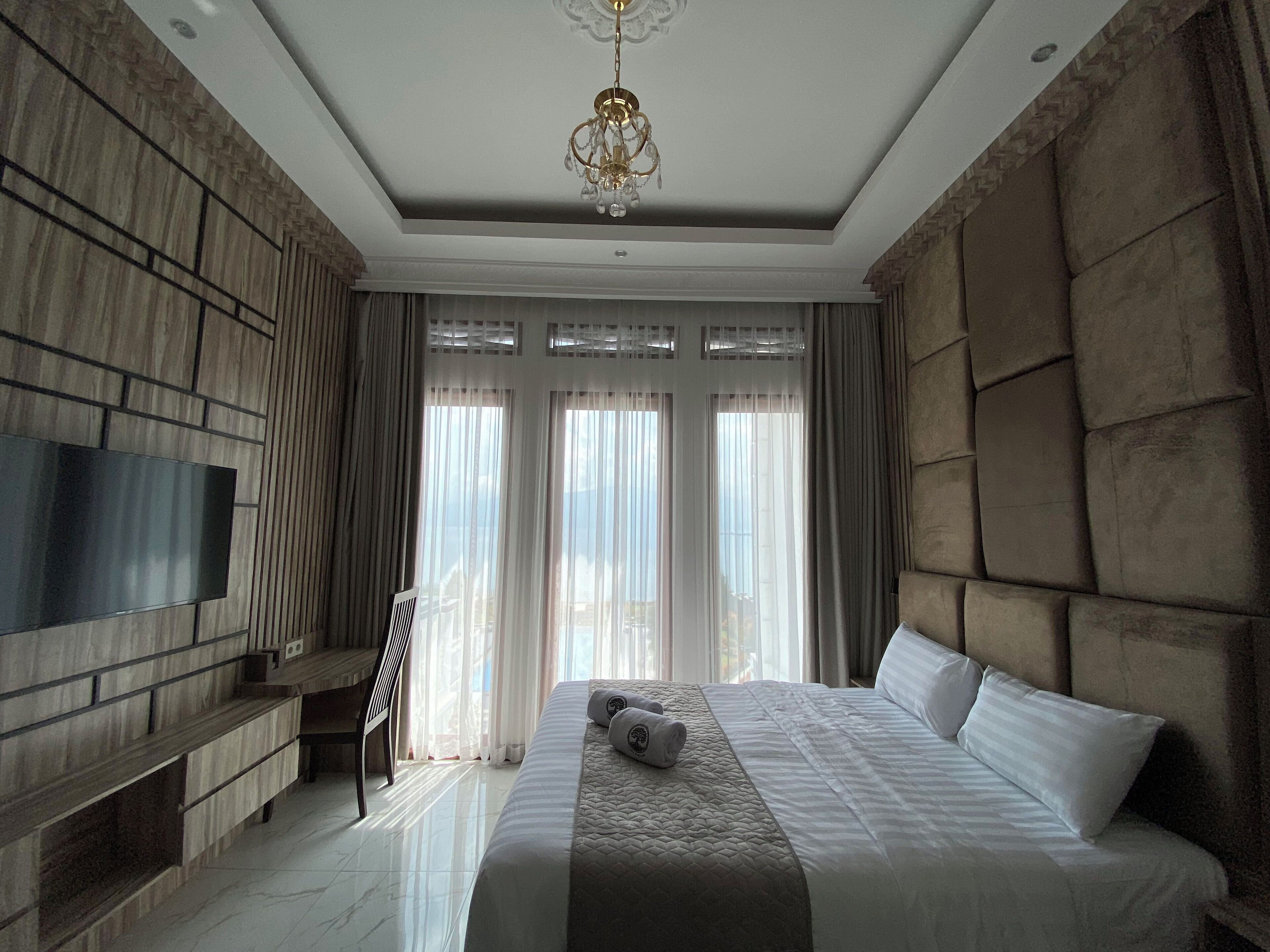 Quarto de hotel moderno com uma cama grande, televisão de tela plana na parede e um candelabro.
