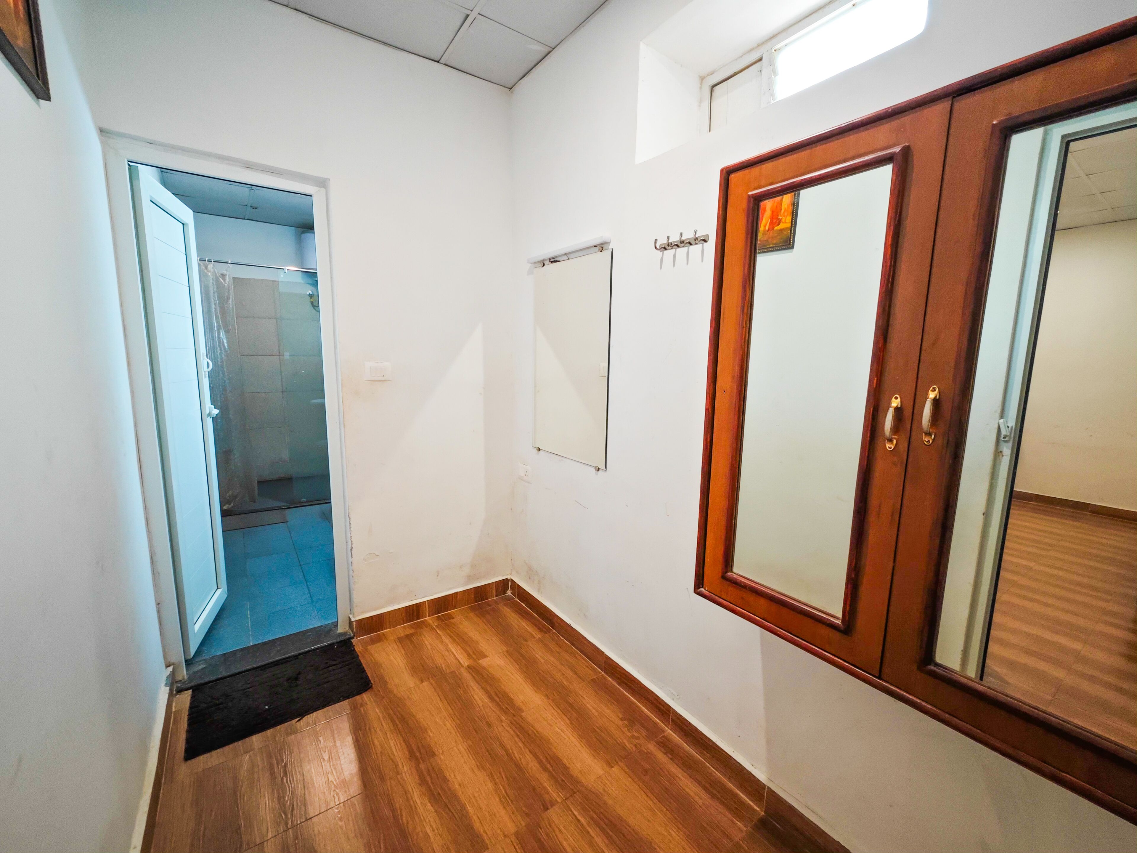 Um corredor com piso de madeira, uma porta com espelho e um interruptor de luz na parede.