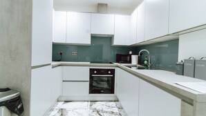 Uma cozinha moderna com armários brancos, forno embutido e bancada de mármore.