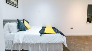 Cama bem arrumada com roupa de cama branca, cabeceira cinza e almofadas decorativas.