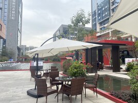 Uma área externa com assentos, cadeiras de vime e mesas, um recurso de água e vista para edifícios ao redor.