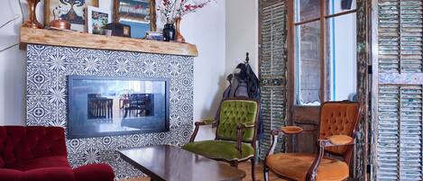 Sala de estar com televisão, sofá vermelho, poltronas verdes e laranja, e uma estante de madeira com objetos decorativos.