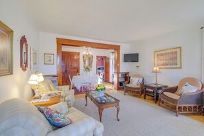 Uma sala de estar com sofá, poltronas, mesa de centro e um canto de jantar com mesa e cadeiras.