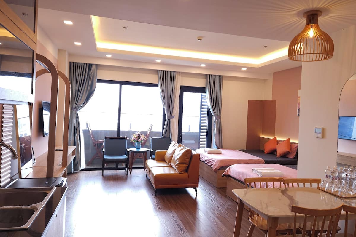 Quarto de hotel moderno com sofá, mesa de jantar com cadeiras, televisão e varanda com vista.