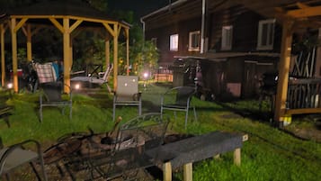 Um gazebo de madeira com cadeiras, churrasqueira e gramado.
