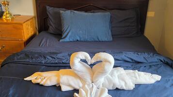Cama com colcha azul, duas almofadas e arranjo de toalhas decorativo em forma de cisnes.