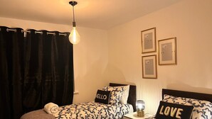 Quarto com duas camas, uma mesa de cabeceira, um abajur e uma cortina.
