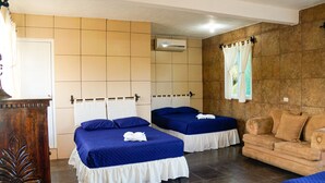Quarto de hotel com duas camas, um sofá e uma cômoda de madeira.