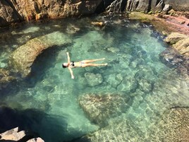Uma pessoa flutua em uma piscina cristalina, rodeada por terreno rochoso.