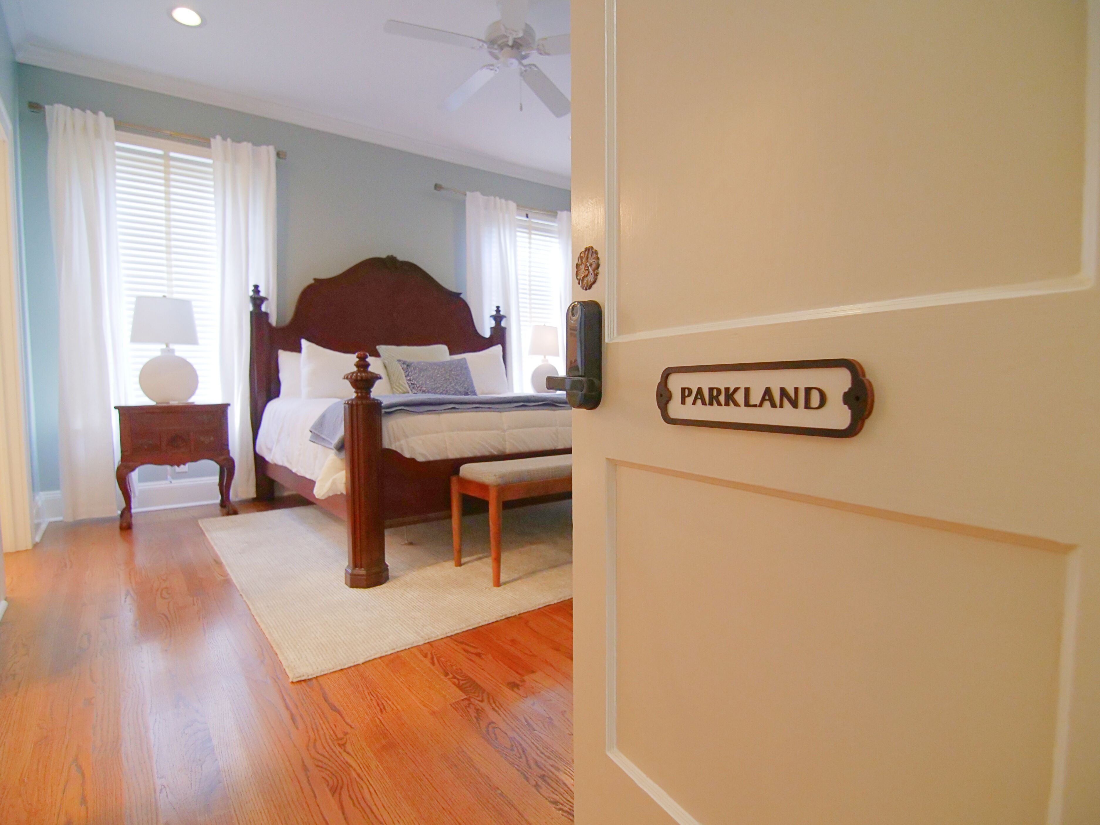 Quarto com cama de madeira, mesa de cabeceira, luminária e uma placa com a inscrição 'PARKLAND'.
