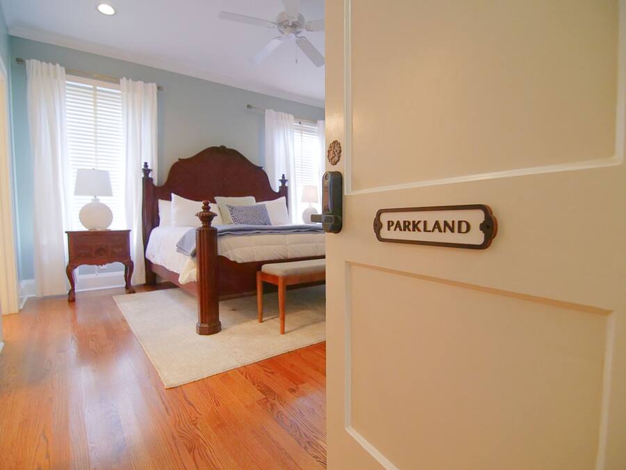 Quarto com cama de madeira, mesa de cabeceira, luminária e uma placa com a inscrição 'PARKLAND'.