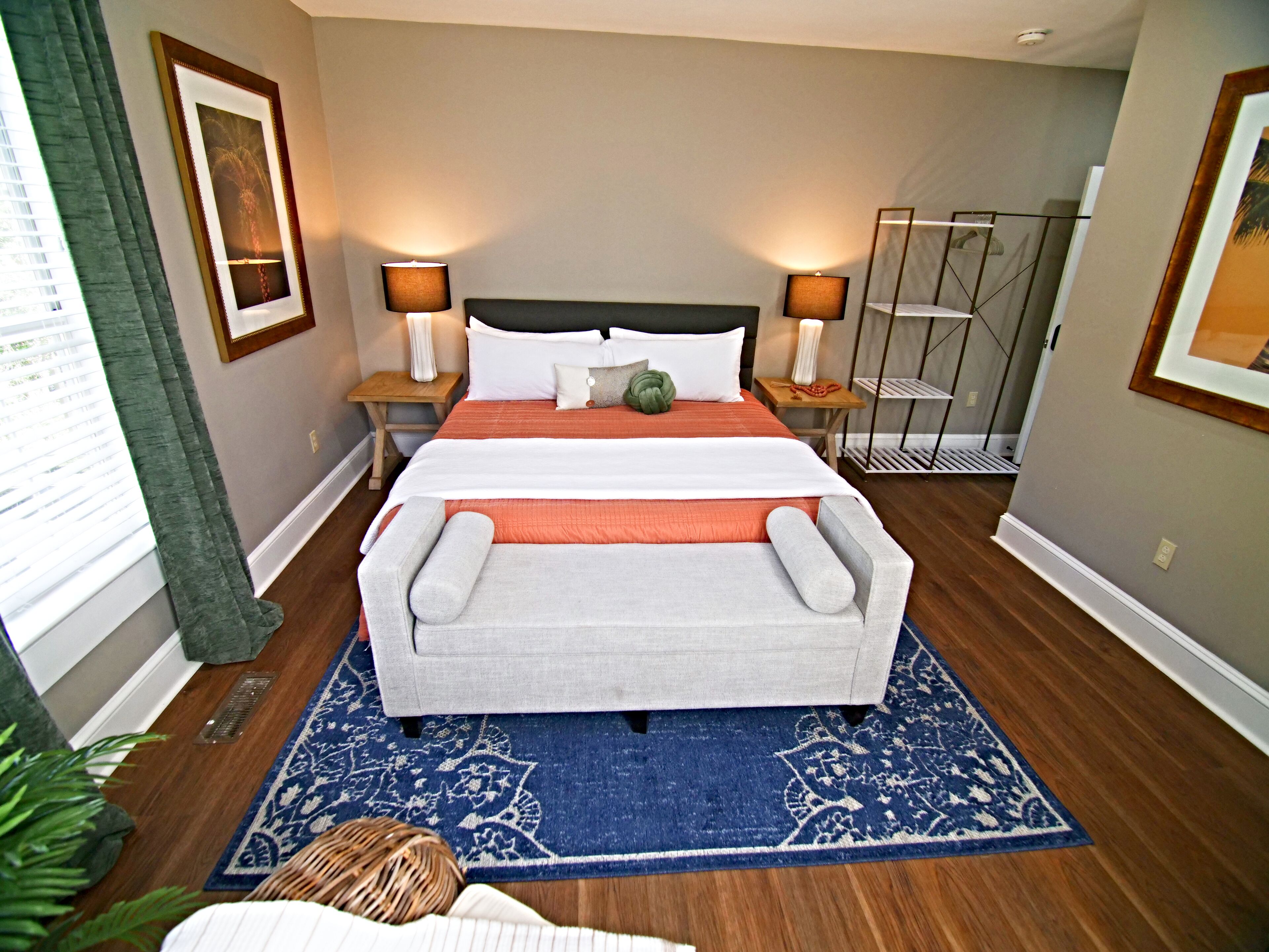 Quarto bem arrumado com uma cama grande, duas mesas de cabeceira, um criado-mudo, um tapete azul estampado e piso de madeira.