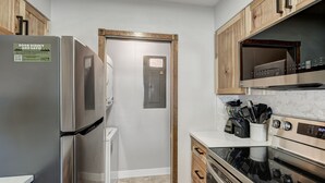 Cozinha equipada com frigorífico de aço inoxidável, micro-ondas e forno. Apresenta bancada branca e armários de madeira.