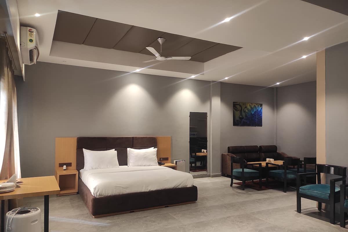 Quarto de hotel moderno com uma cama grande, um ventilador de teto, um espaço de estar com cadeiras e um quadro na parede.