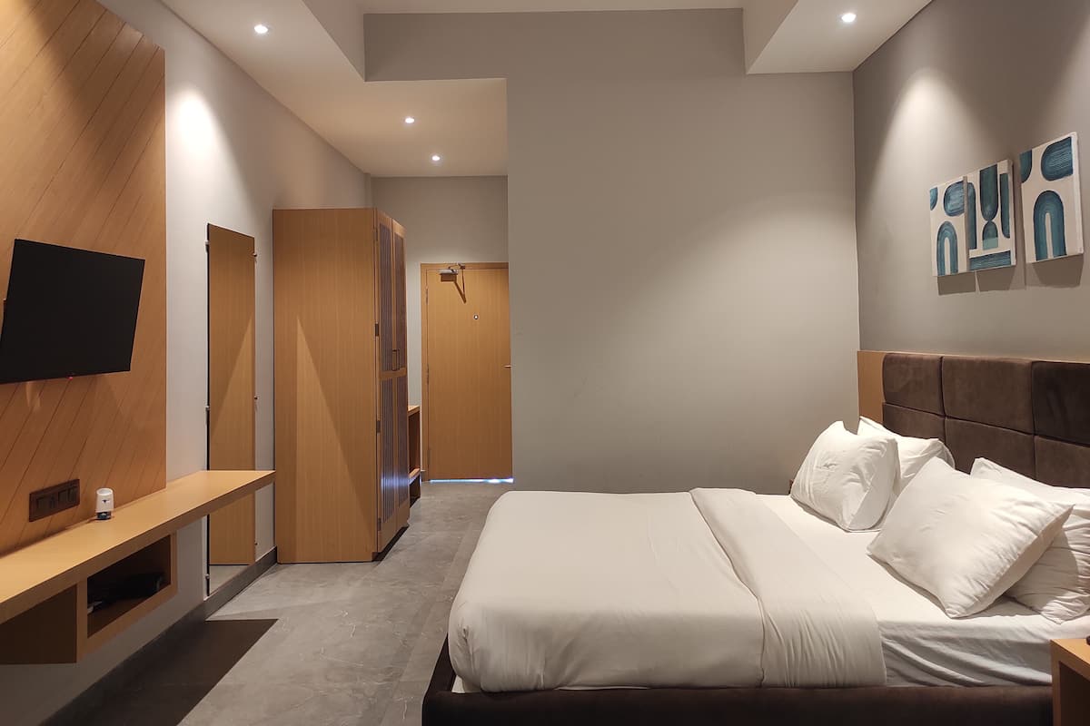 Quarto de hotel moderno com cama, mesas de cabeceira, televisão e guarda-roupa.