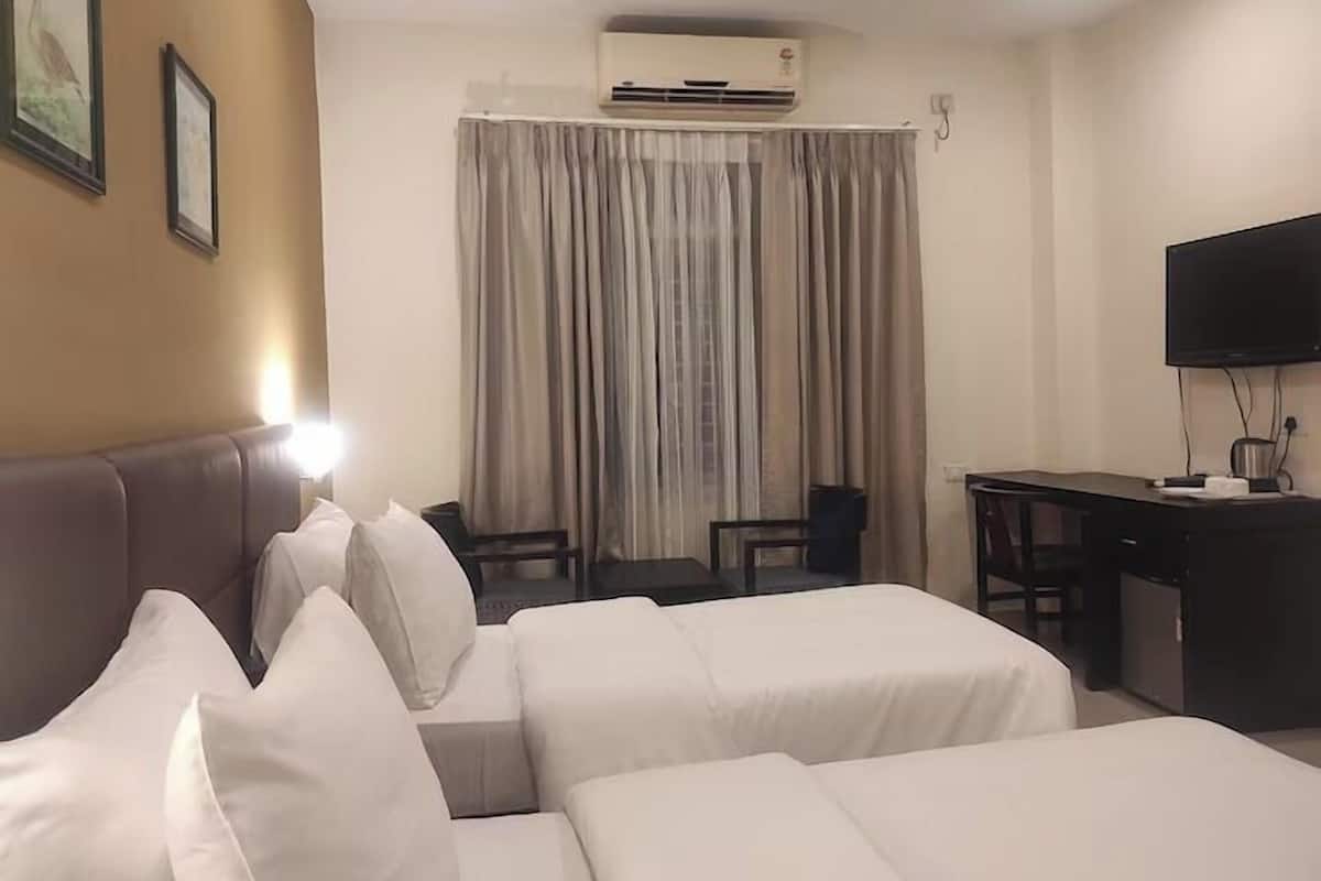 Quarto de hotel com duas camas, uma escrivaninha, uma cadeira, uma televisão e um aparelho de ar condicionado.