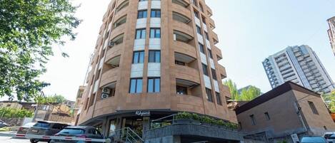 Um hotel com vários andares e fachada curva, estacionamento externo e uma pequena área de entrada com degraus.