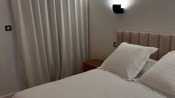 Uma cama bem arrumada com roupa de cama branca, cabeceira e mesa de cabeceira com abajur.